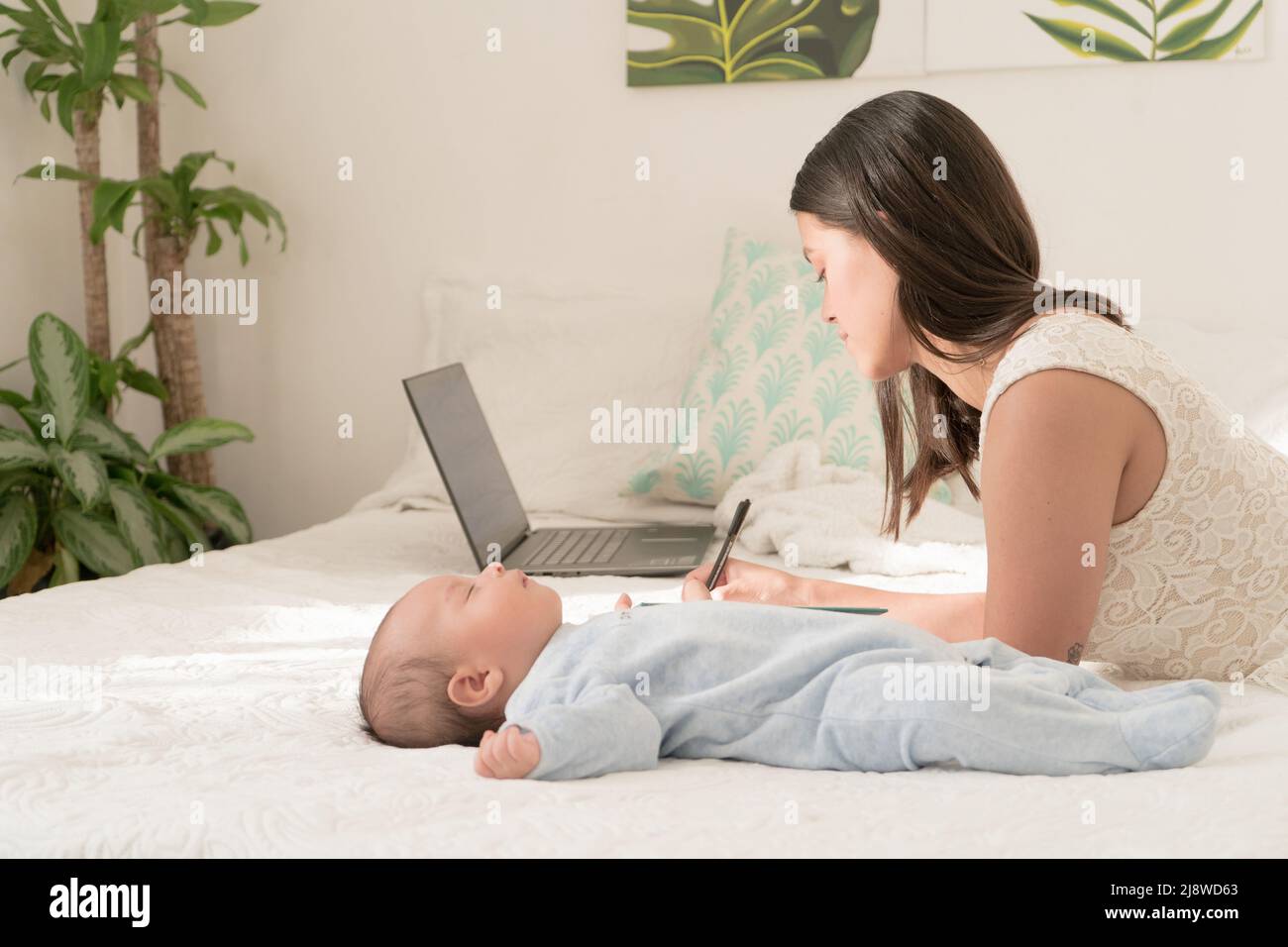 Latin mother is writing side your baby on her bed Stock Photo - Alamy