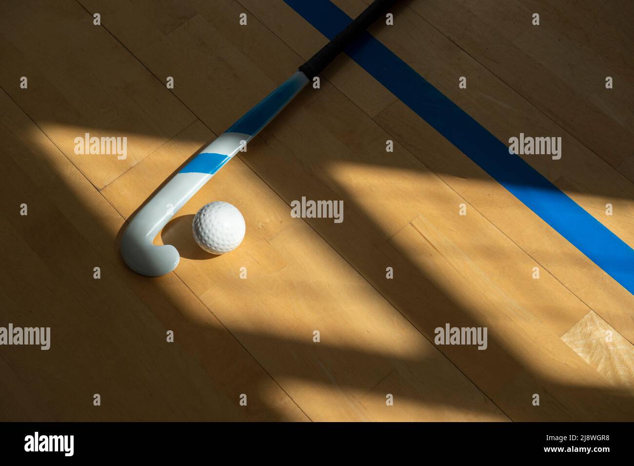 Field hockey stick and white ball with natural lighting on parquet ...