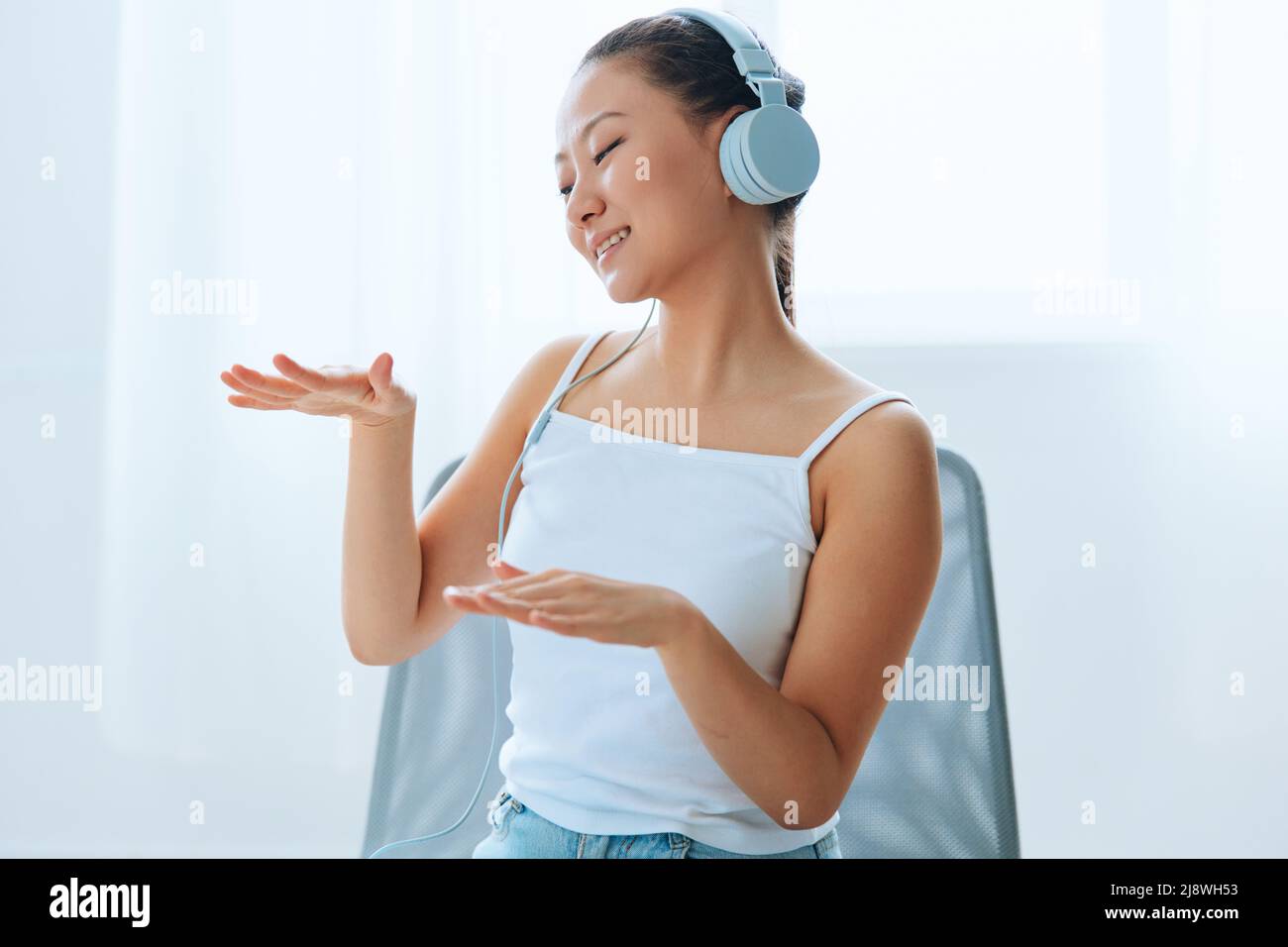 Relaxing dancing cheerful tanned lovely young Asian woman in headphones ...