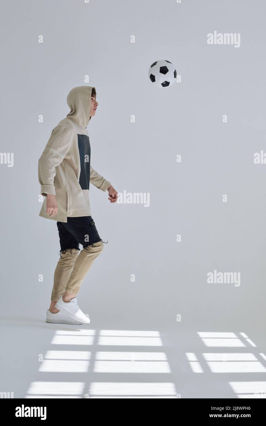 Young sportsman in street style wear training with soccer ball in large ...