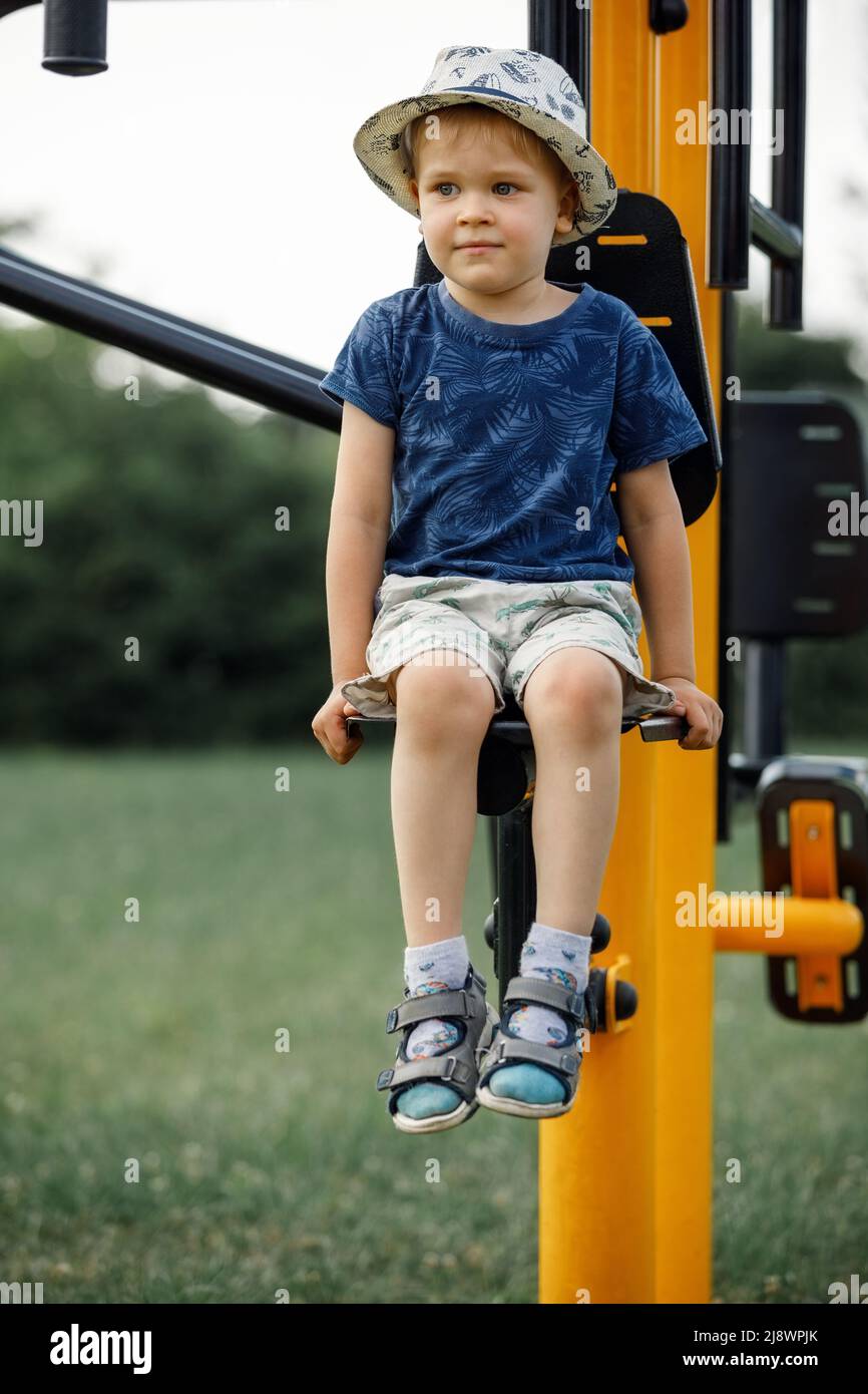 The little boy sitting in on the street exercise machine, child poses ...