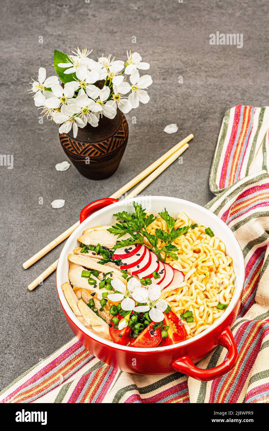 Asian noodles with chicken, vegetables, and herbs in a red bowl ...