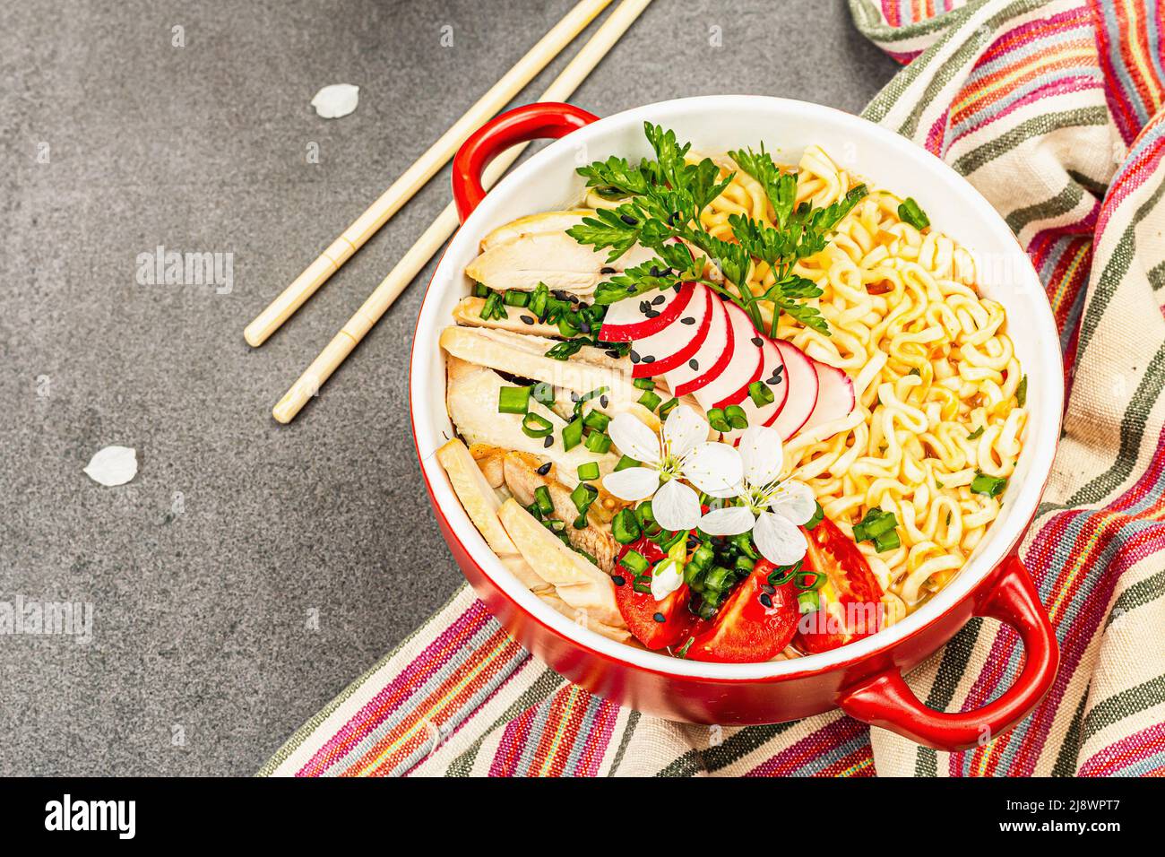 Asian noodles with chicken, vegetables, and herbs in a red bowl ...
