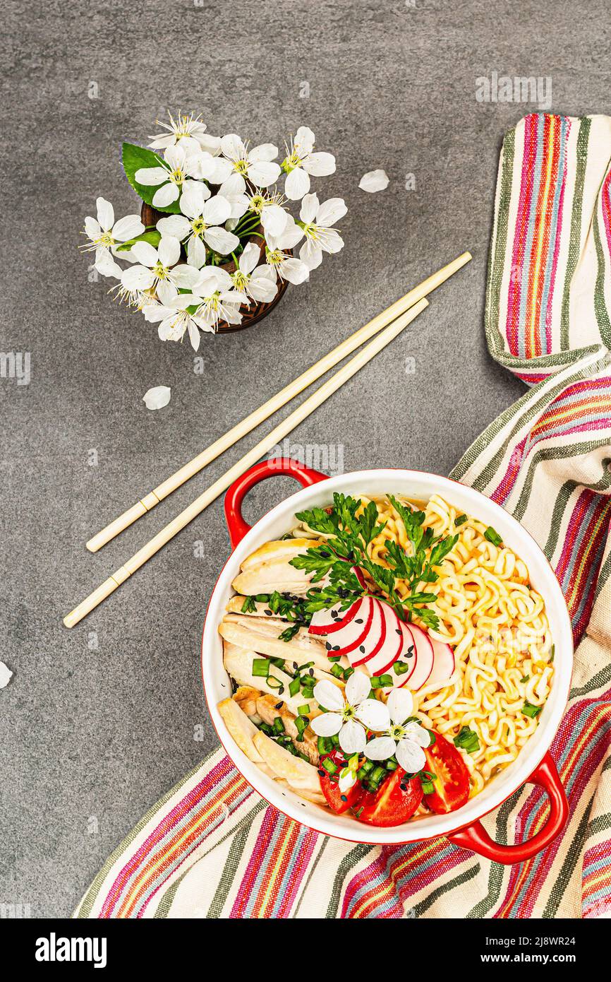 Asian noodles with chicken, vegetables, and herbs in a red bowl ...
