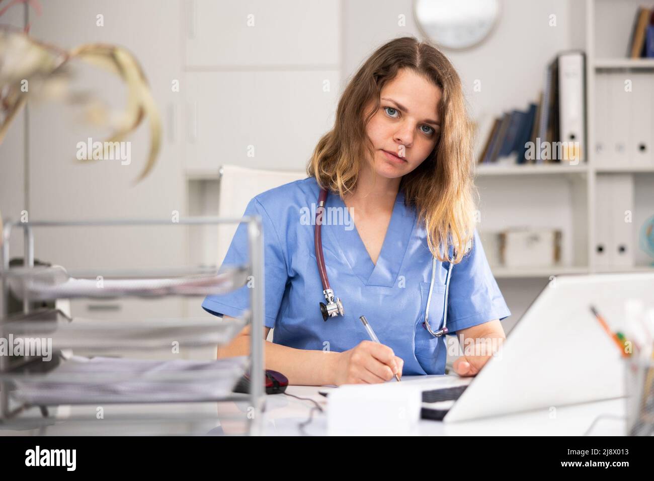 Portrait of female doctor who is working with laptop and documents ...
