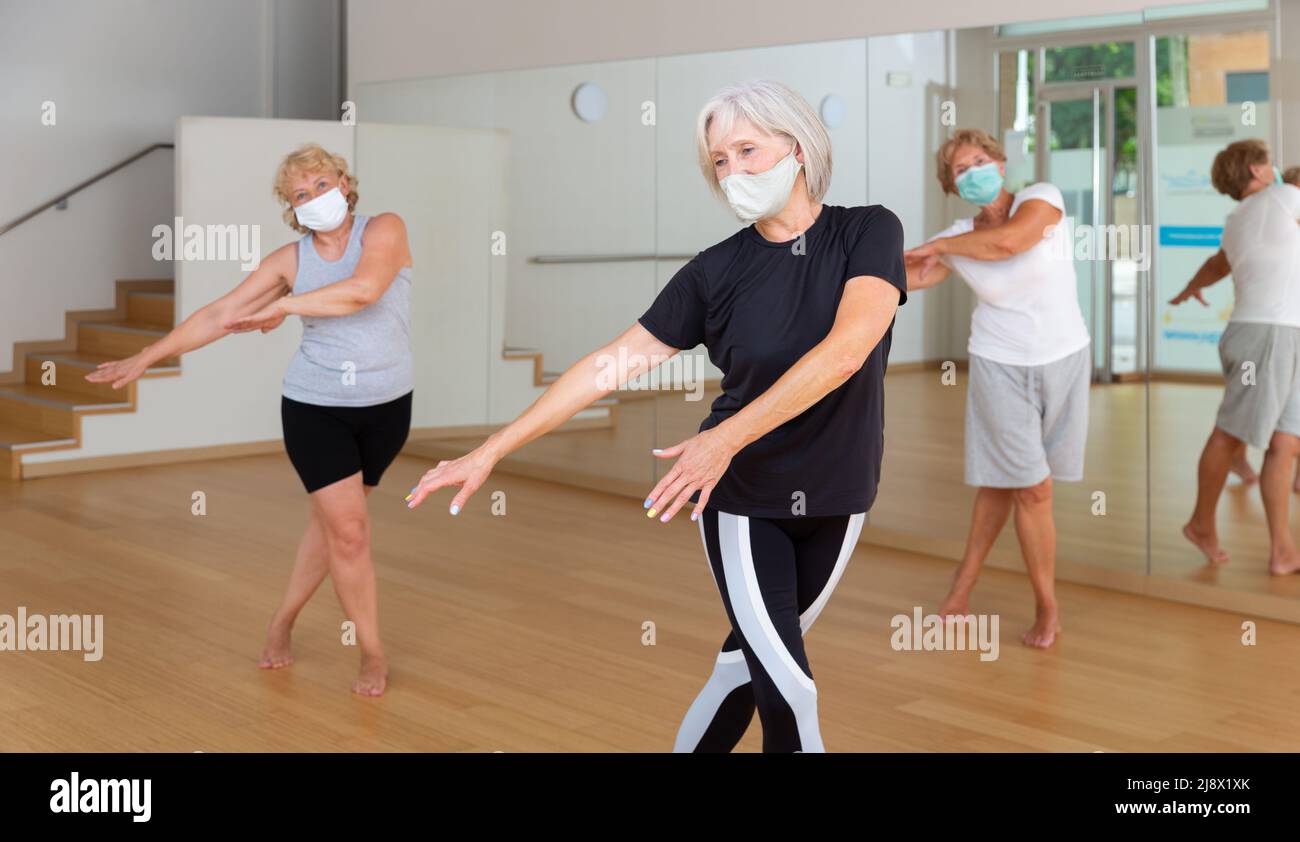 Group of mature women in protective masks are engaged in active dancing ...