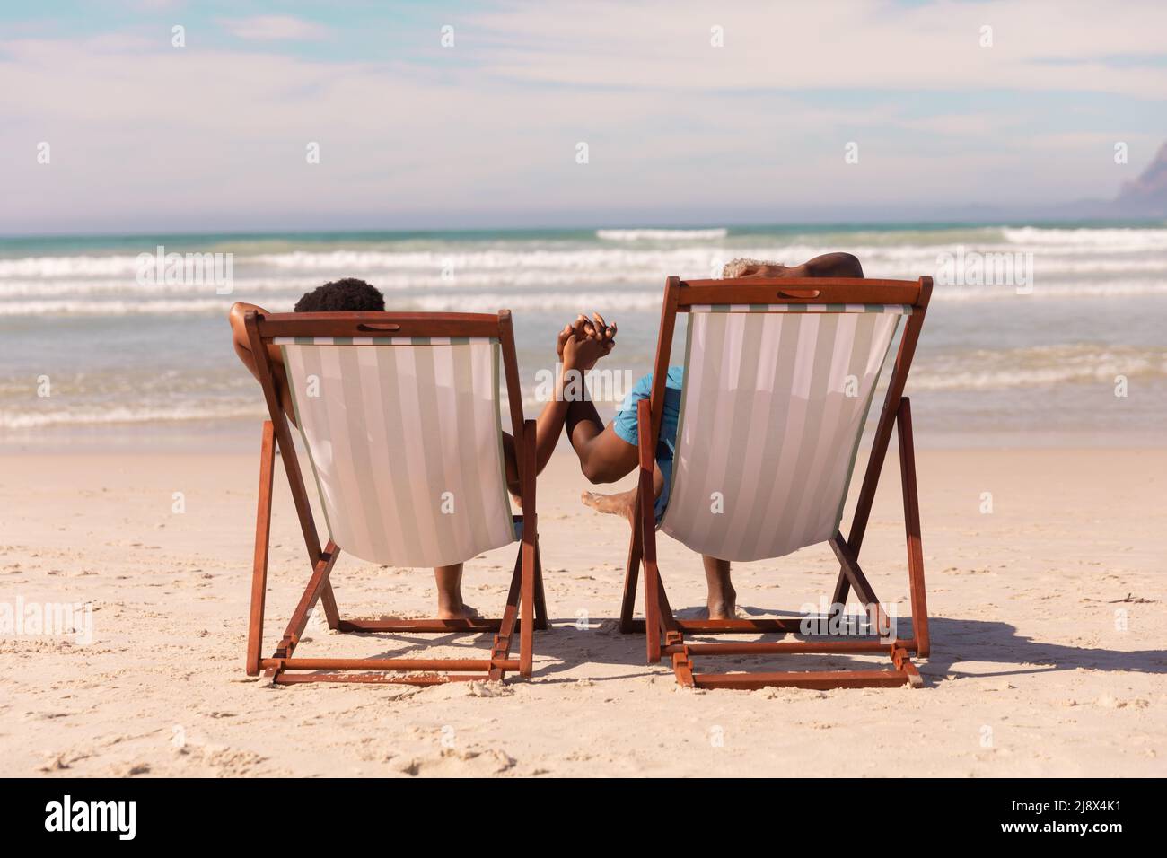 African American Couple Holding Hands While Relaxing On Deckchairs At