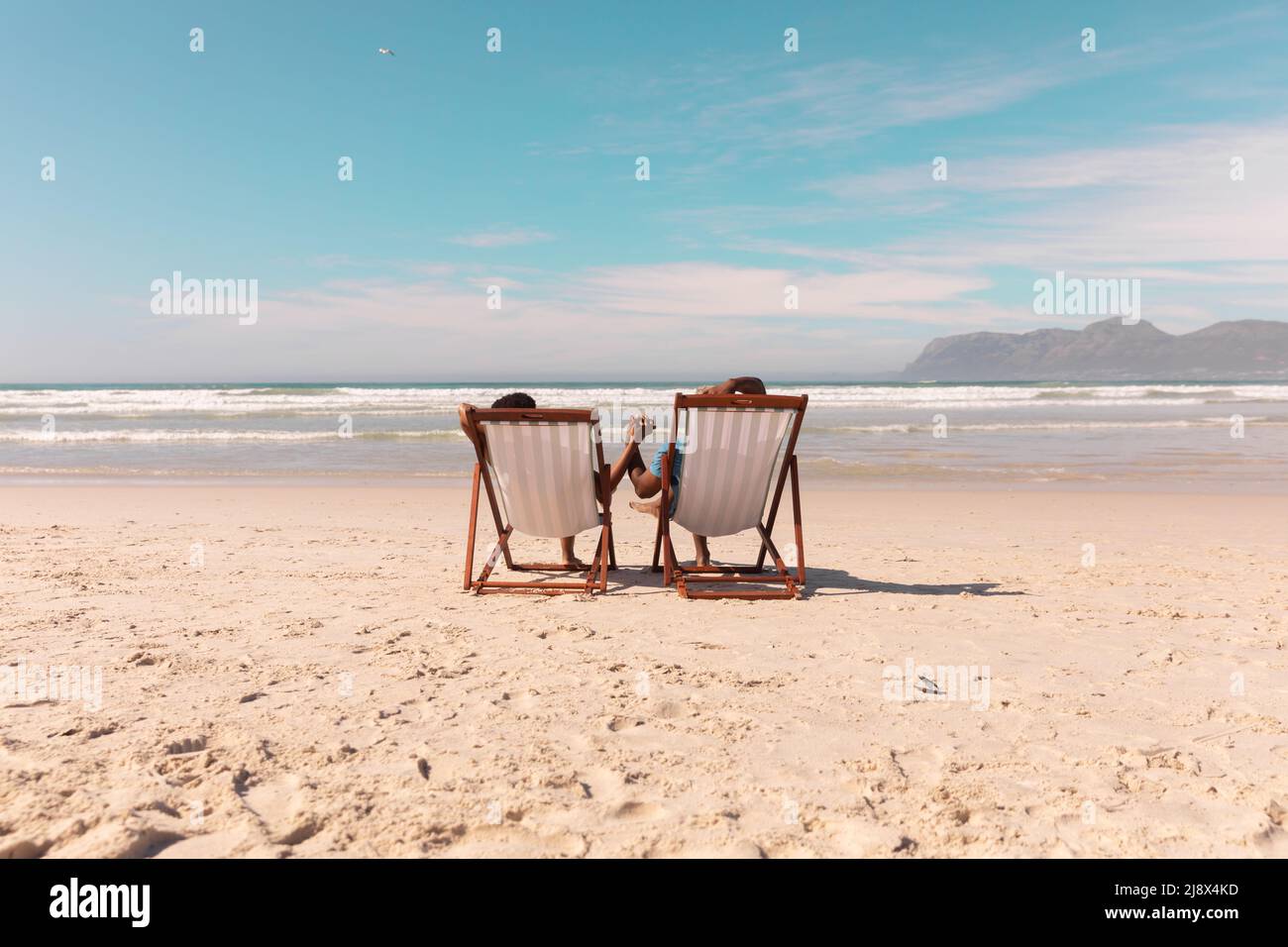 African American Couple Holding Hands While Relaxing On Deckchairs At
