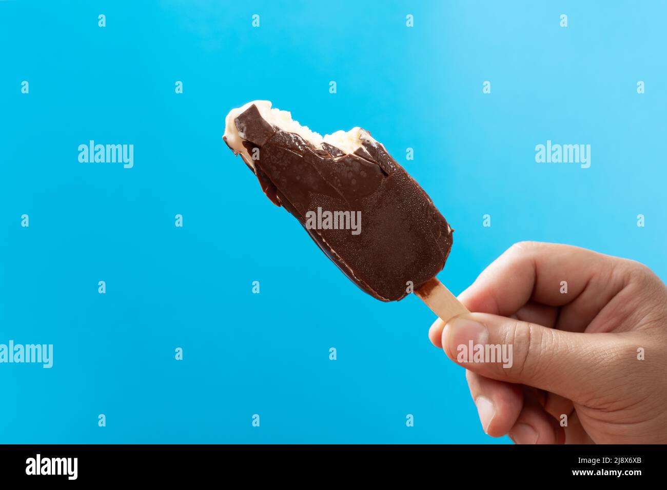 man holding a chocolate outer popsicle with couple of bites on blue ...