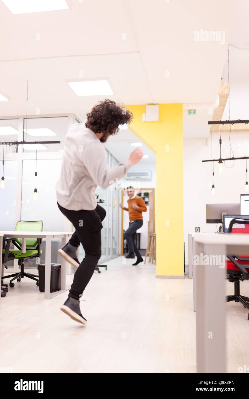 Two businessmen having fun at the office. Friendly colleagues jumping ...