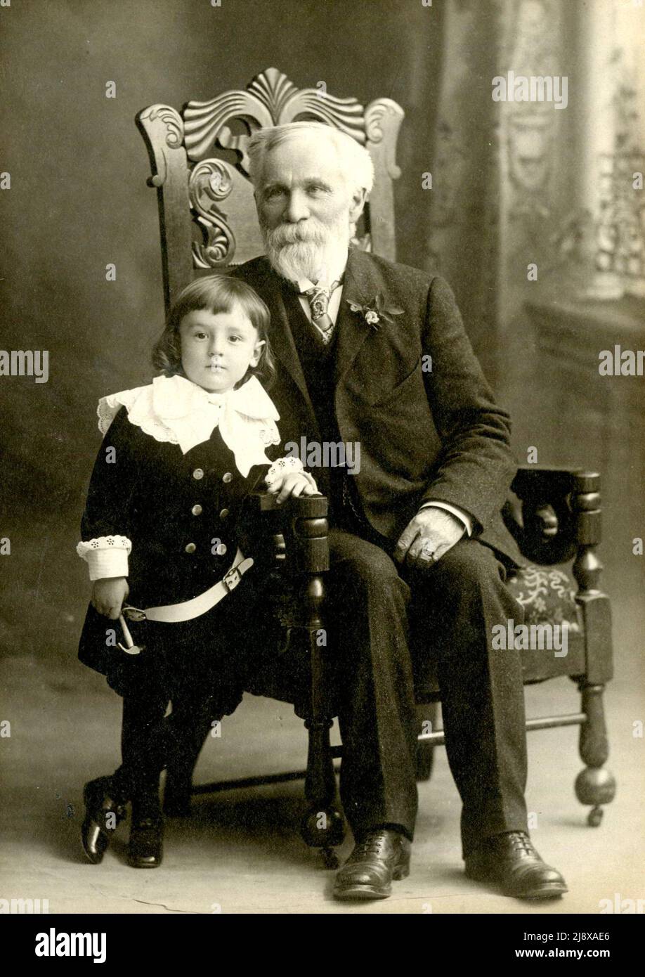 Older man sitting on a chair, with a small child standing next to him ...