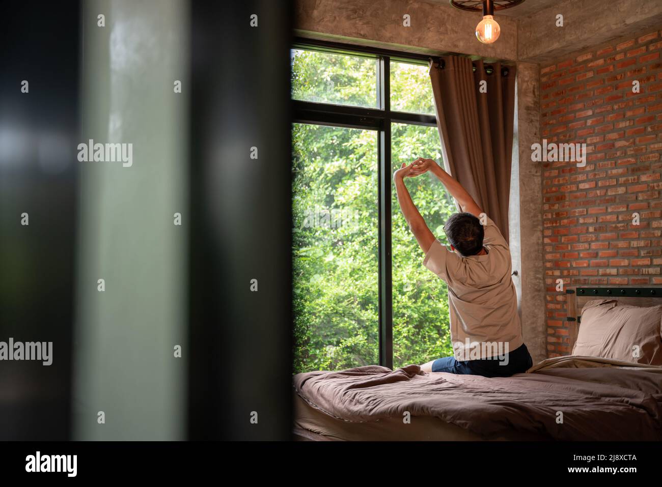 A lazy man happy waking up in the bed rising hands to window in the ...