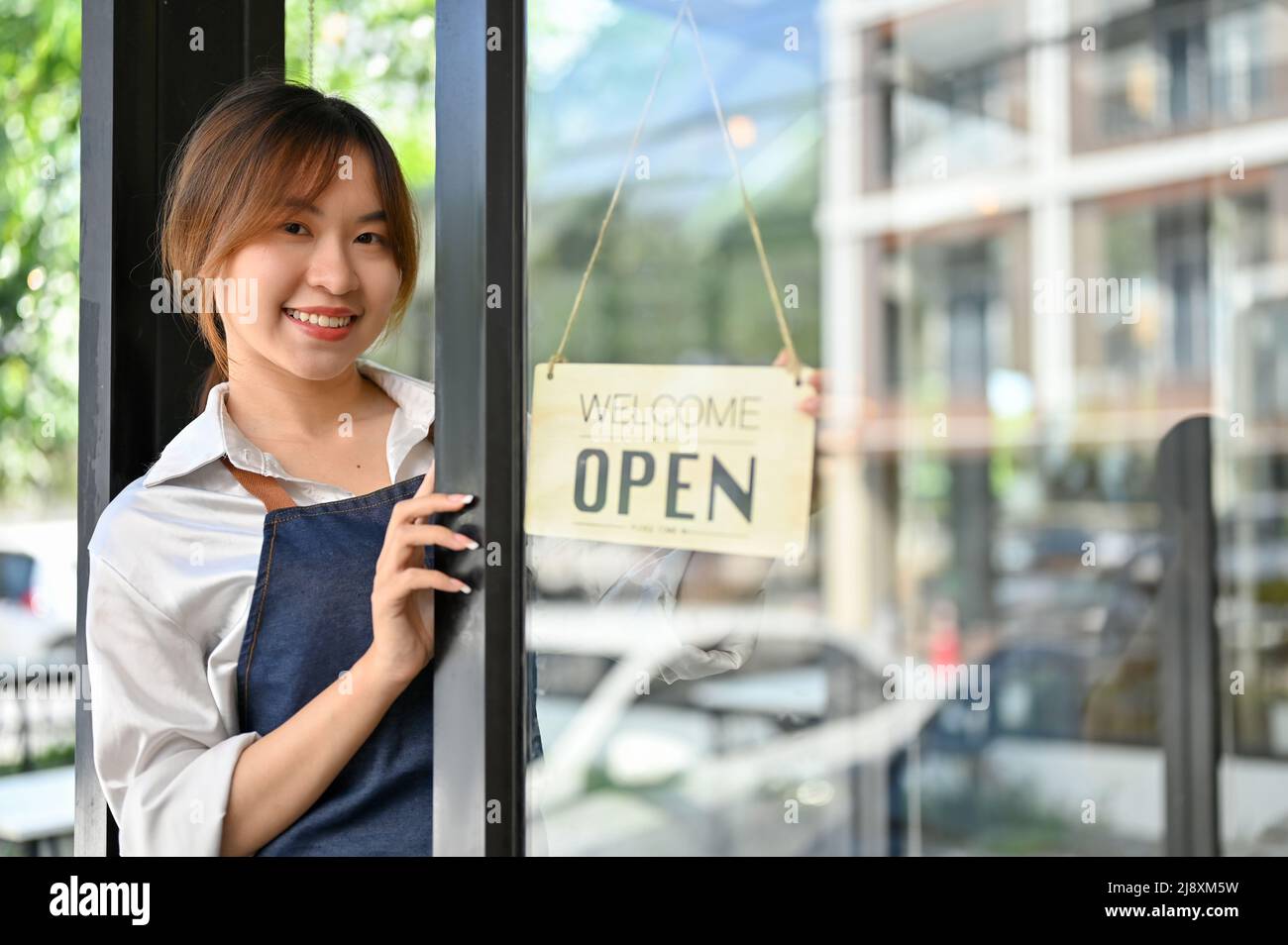 Beautiful Asian young female barista hanging a welcome sign on the door ...
