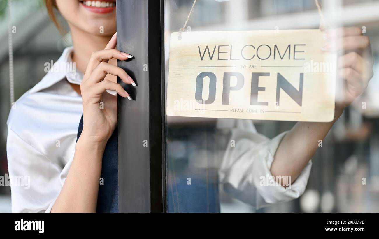 Female barista or coffee shop owner hanging an open welcome sign on the ...
