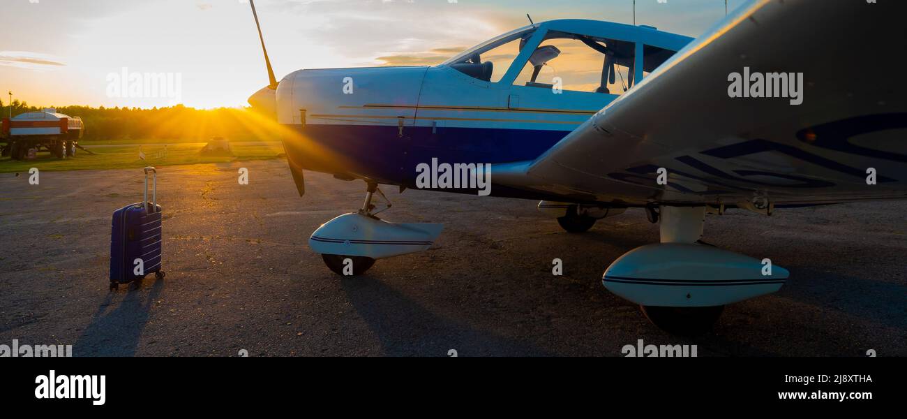 A blue suitcase and a parked small private jet. Quadruple plane with a ...