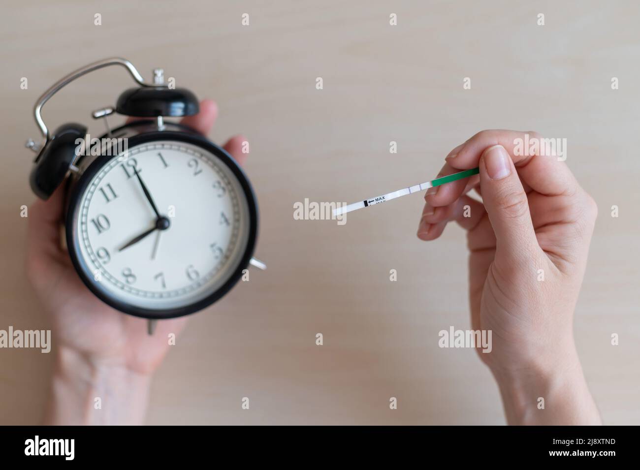Woman holds a positive pregnancy test and alarm clock. Nine months of ...