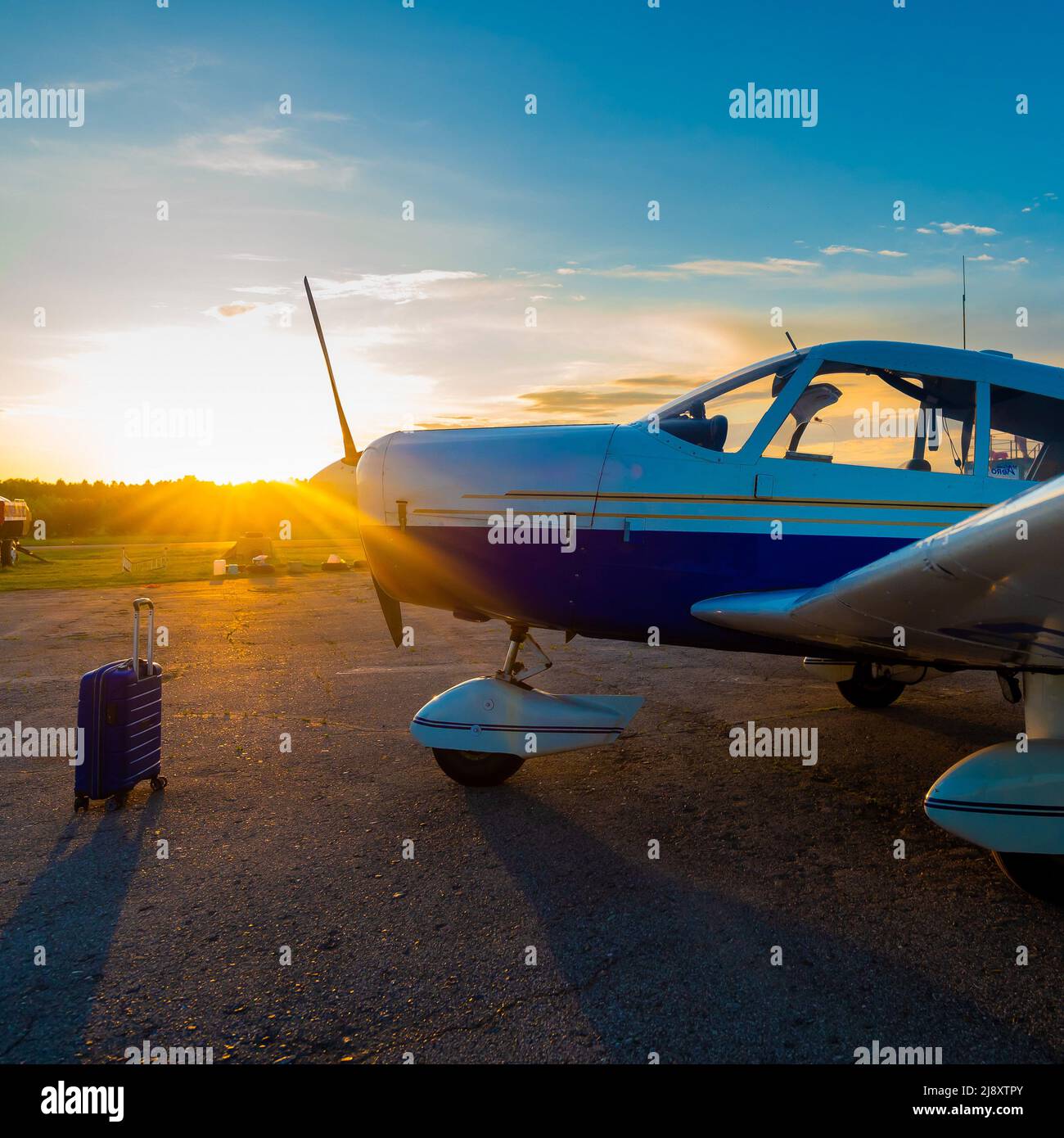 A blue suitcase and a parked small private jet. Quadruple plane with a ...