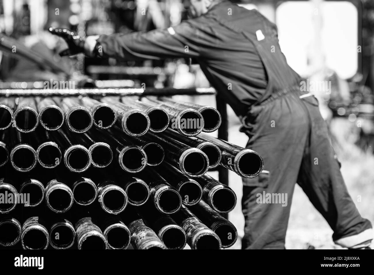 Oil rig drill pipes stacked with oil industry workers in the background ...