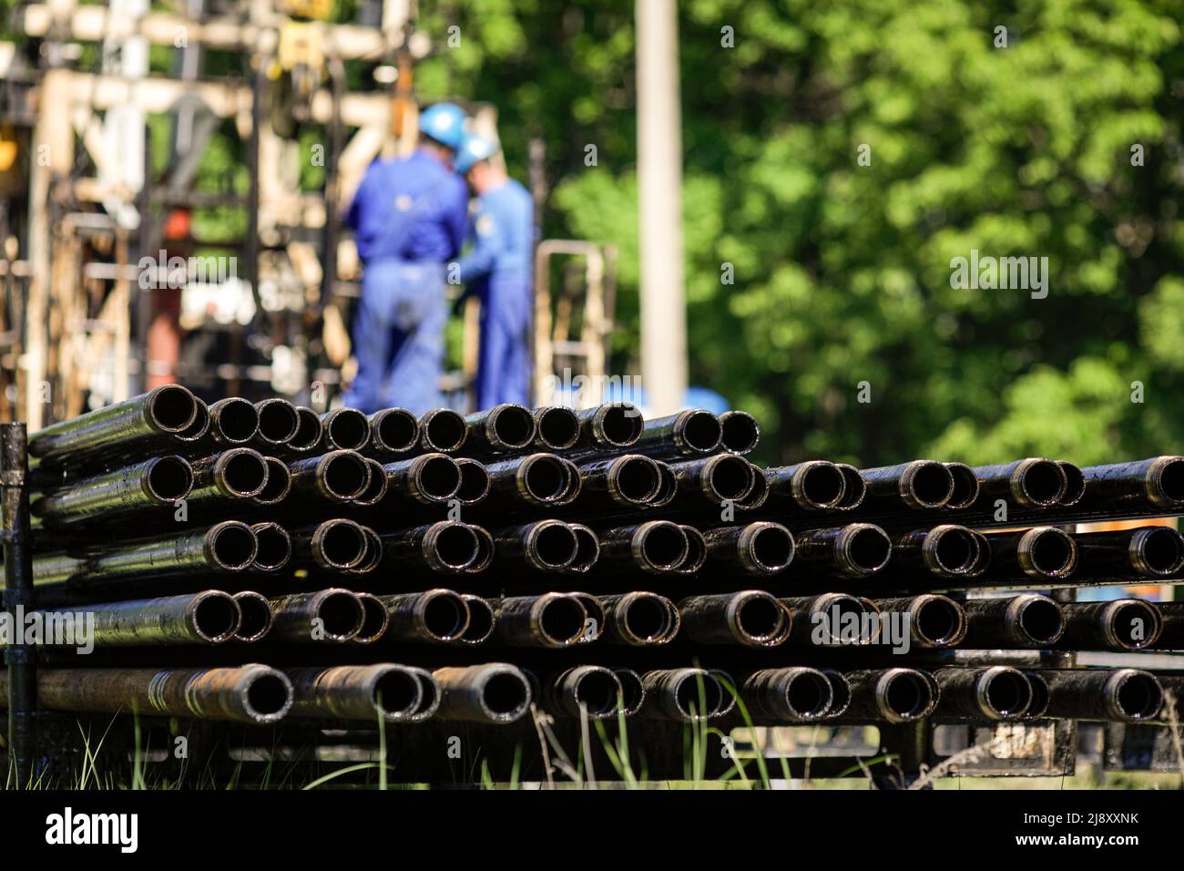 Oil rig drill pipes stacked with oil industry workers in the background ...