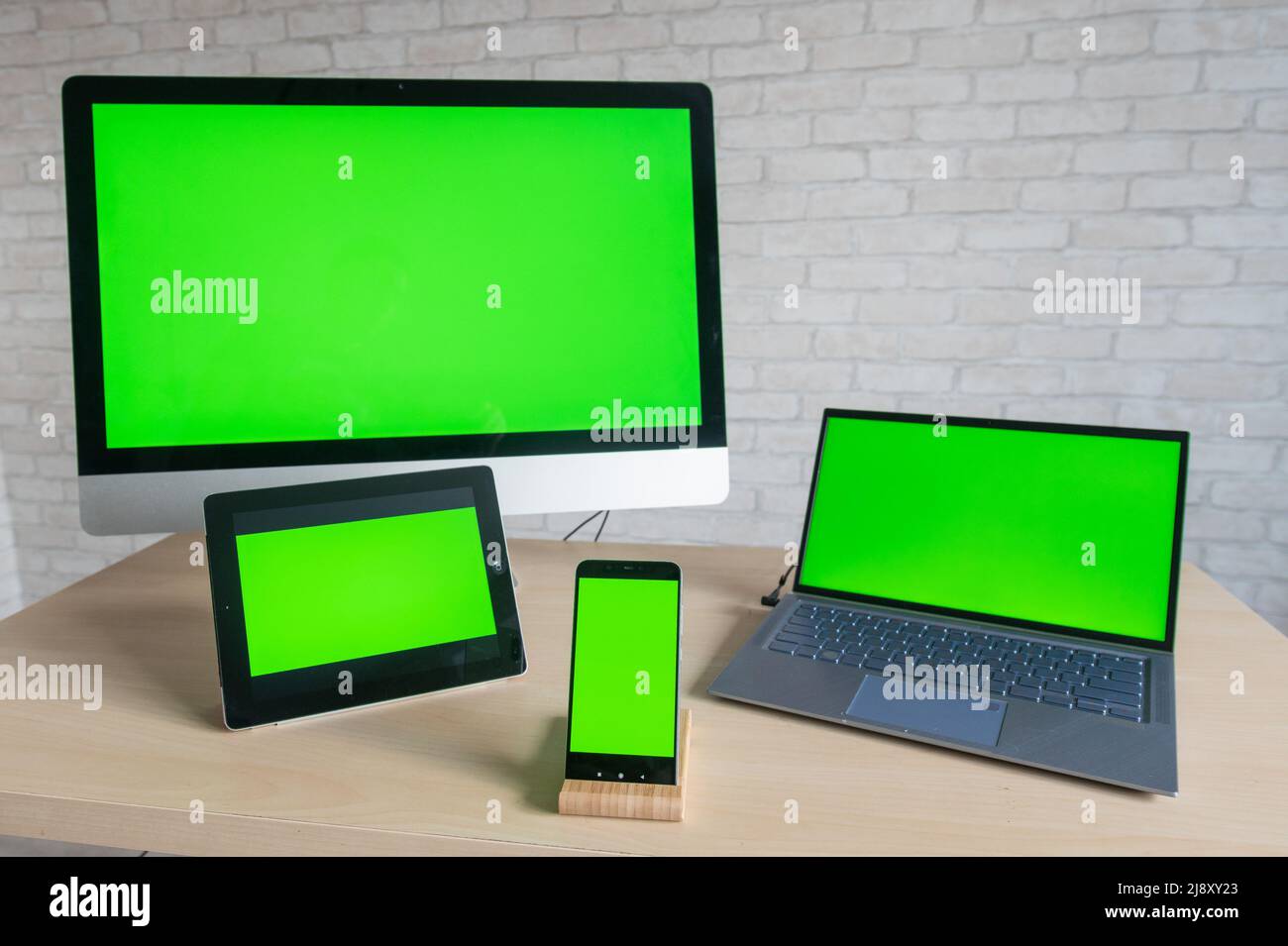 On the table are a computer laptop digital tablet and a phone with green screens on a brick wall ...