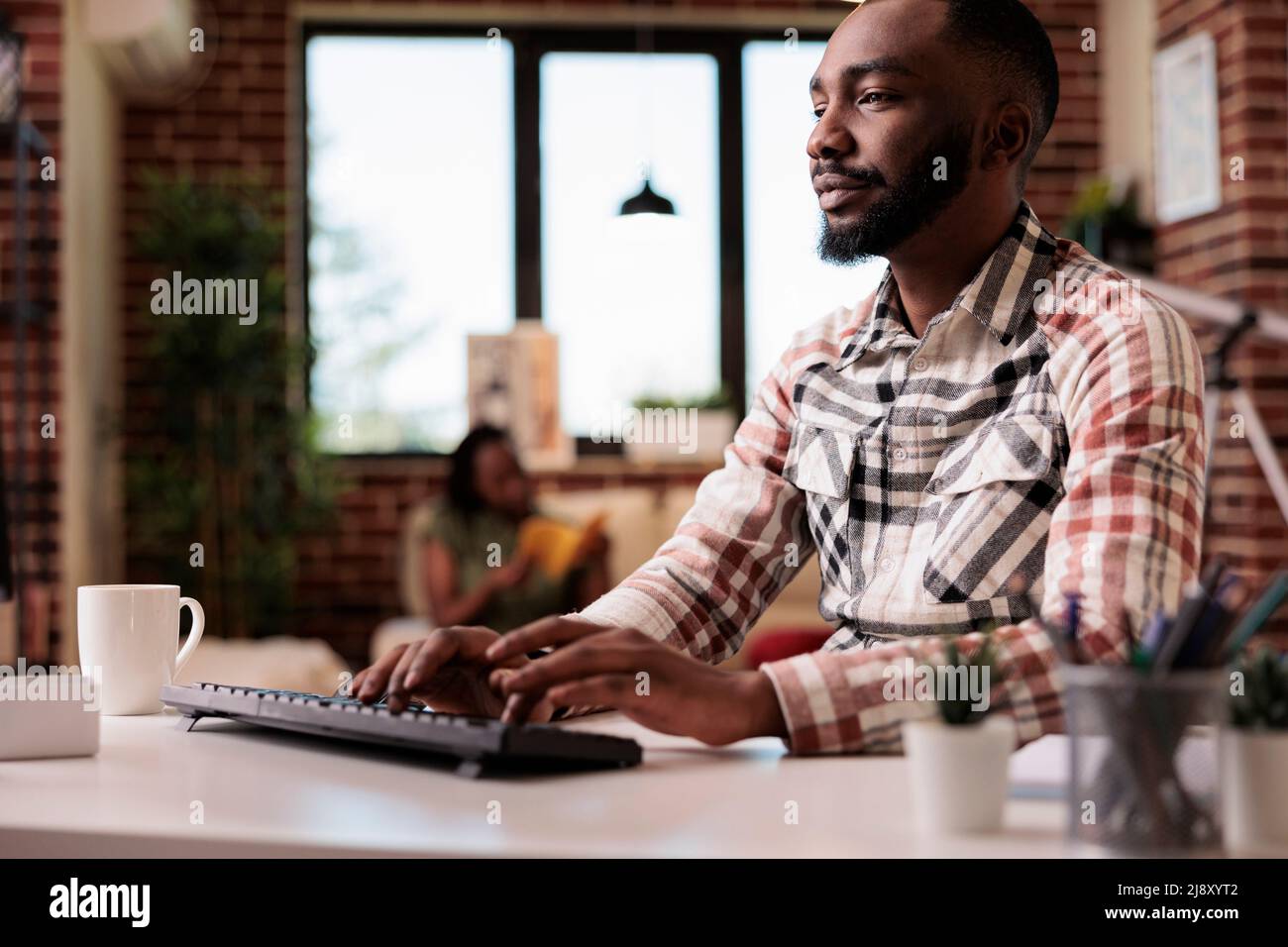 Casual freelancer typing on computer keyboard while looking at screen working from home living ...