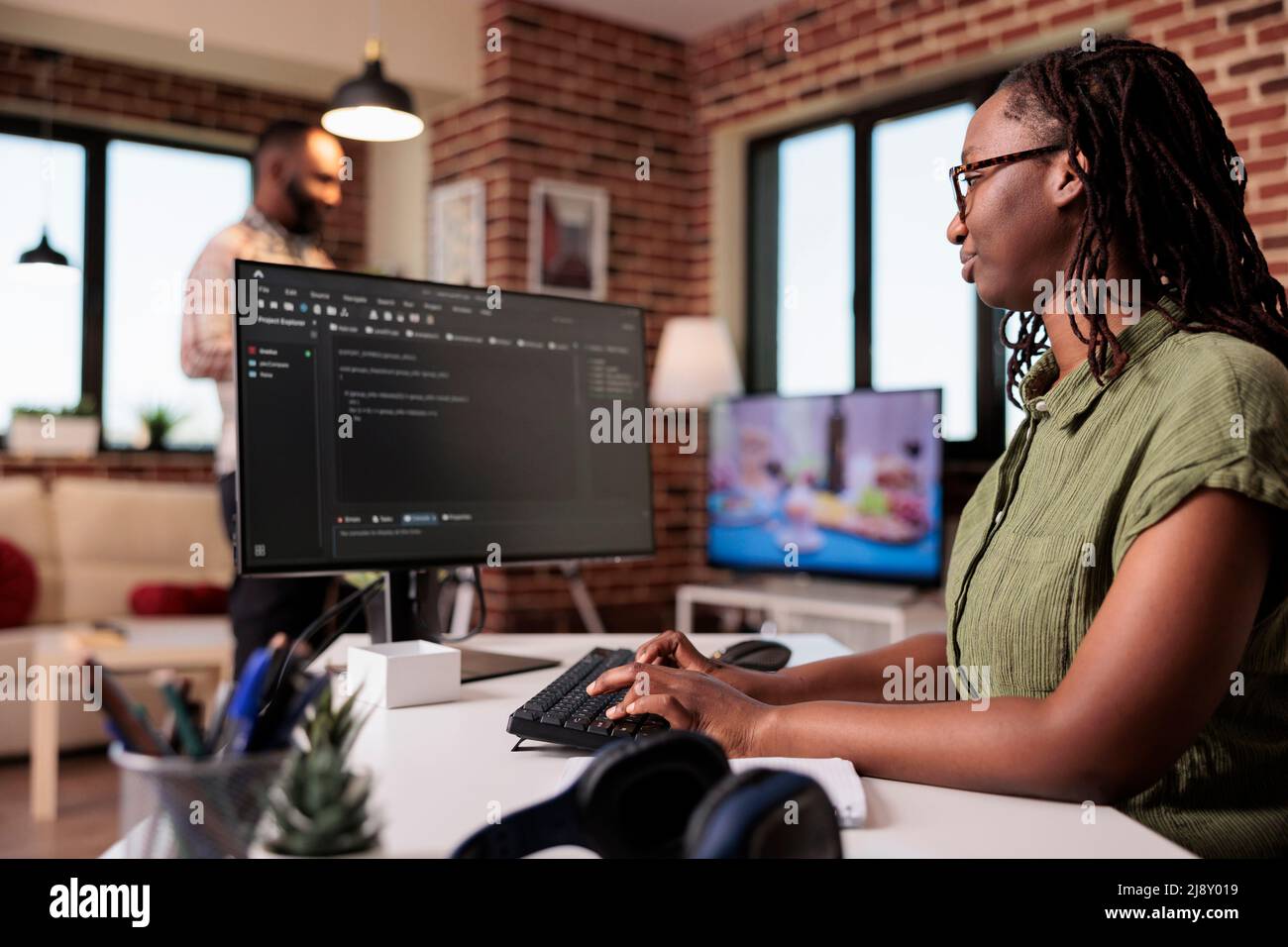 Woman programmer working remote writing code using computer while boyfriend is relaxing watching ...
