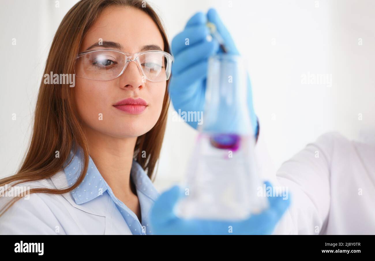 Scientist coworkers in glove add pink liquid to flask, microbiology ...
