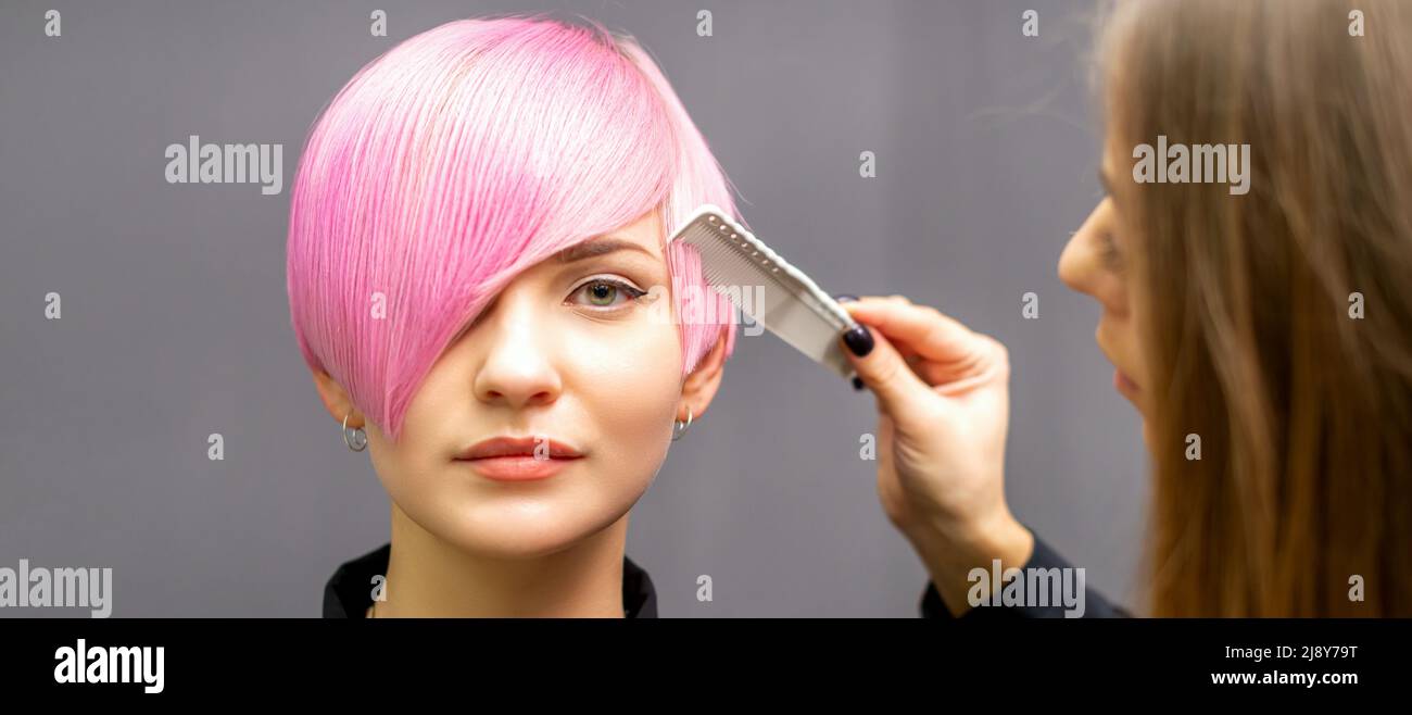 The female hairdresser is combing the dyed pink short hair of the young ...