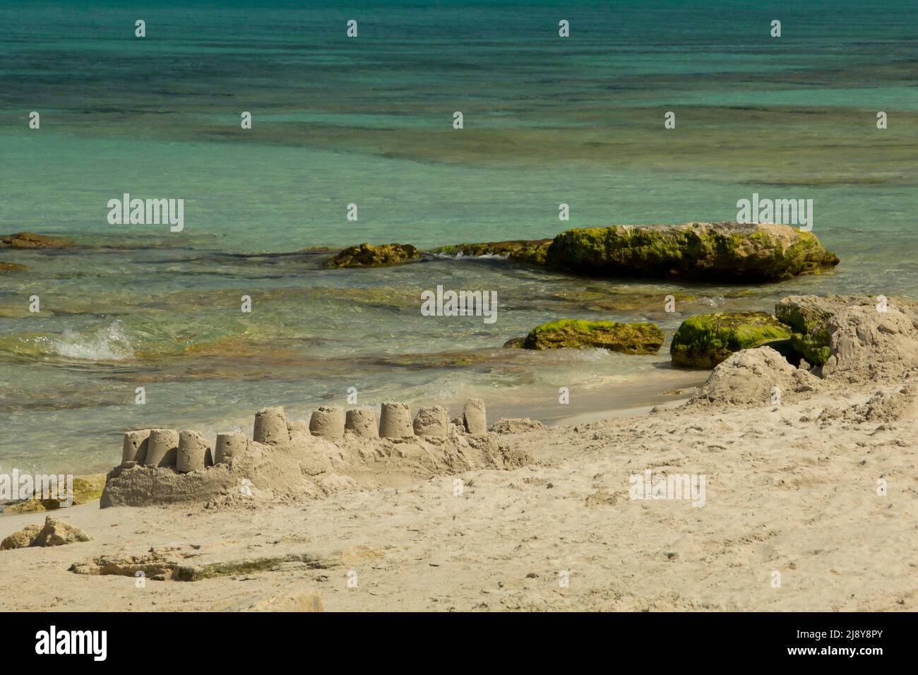 Sand castle wall with green rocks and water in the background at a ...