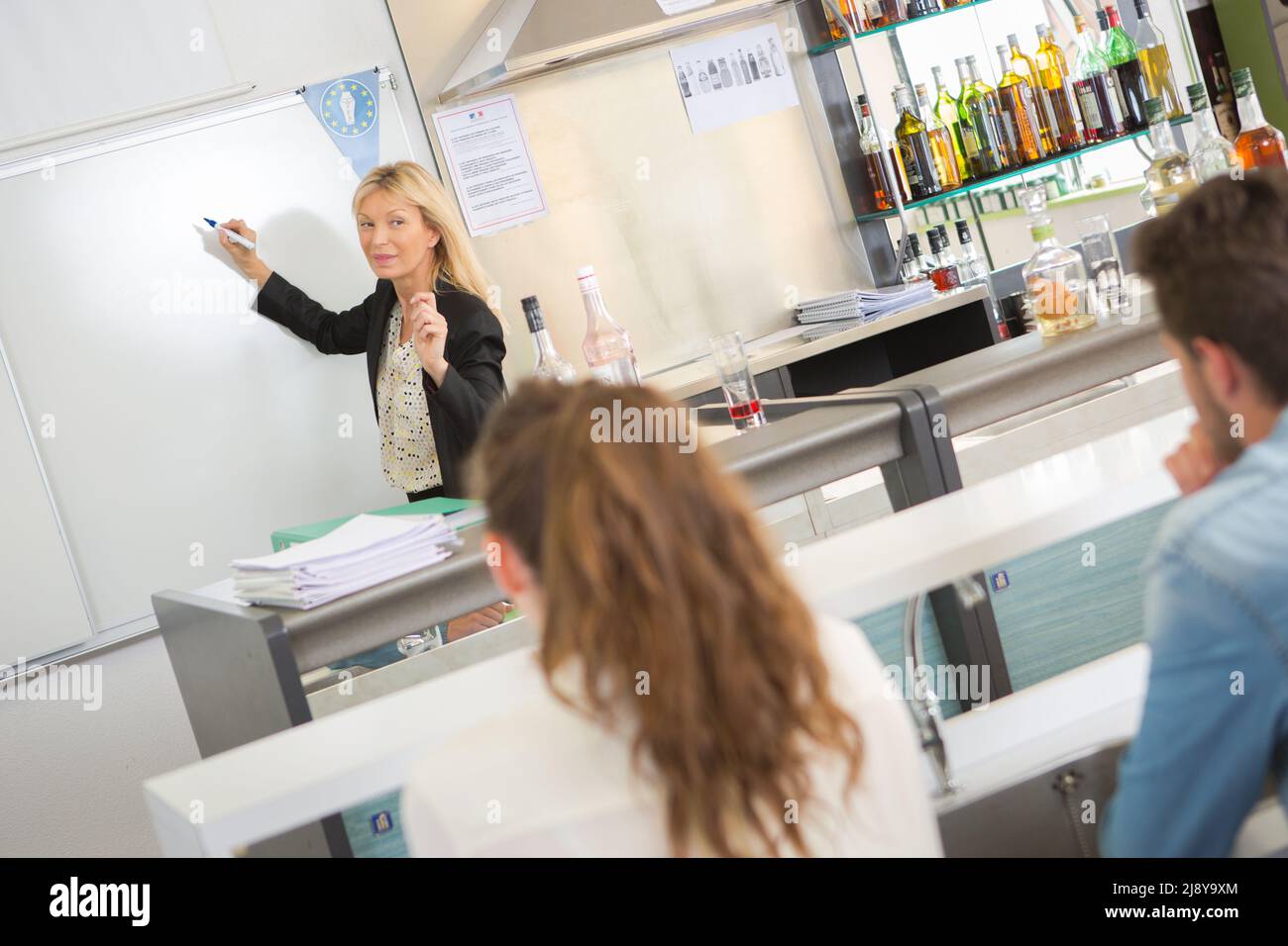 portrait of confident female teacher with students writing in classroom ...