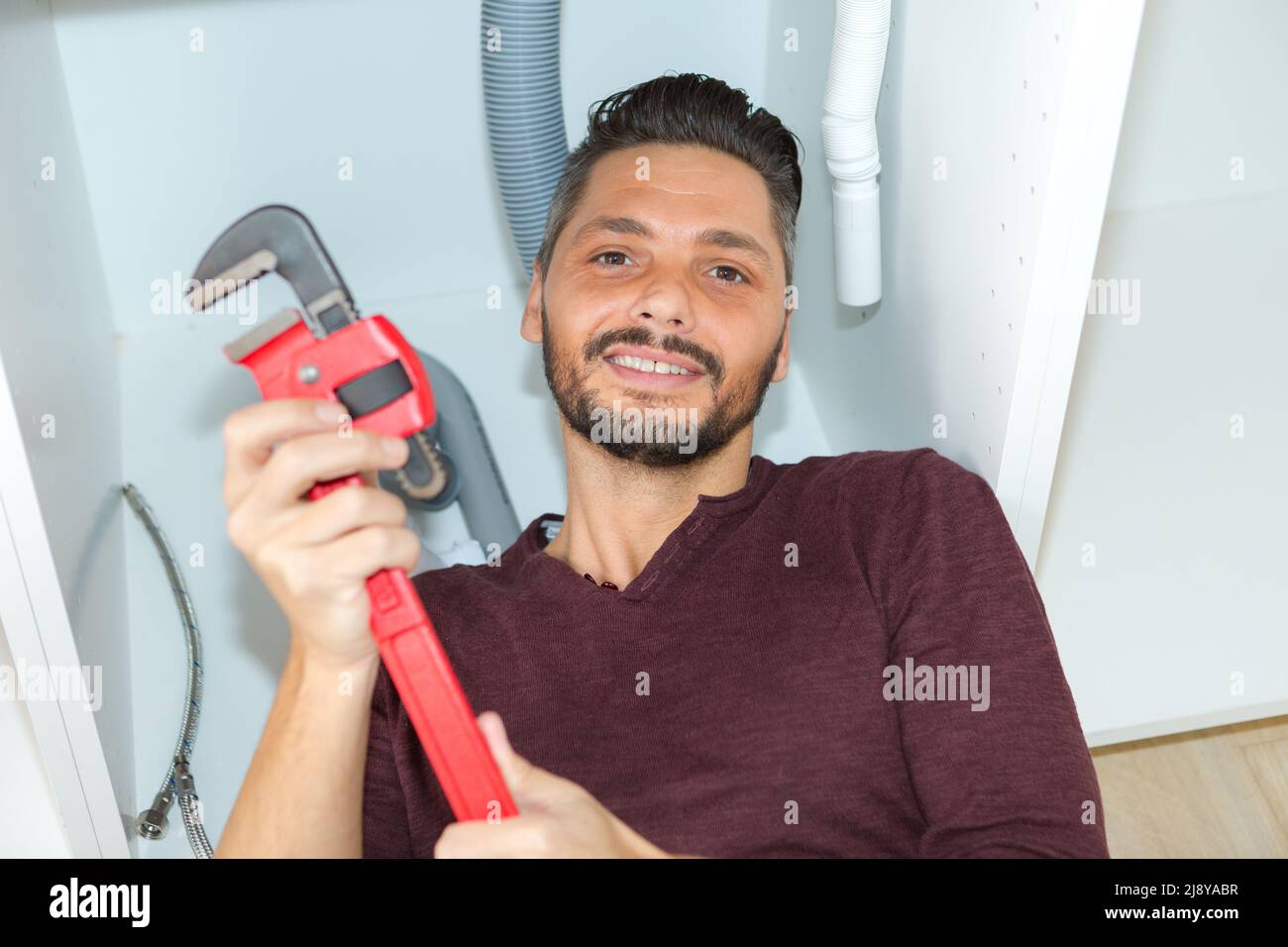 portrait of man under sink holding adjustable wrench Stock Photo - Alamy