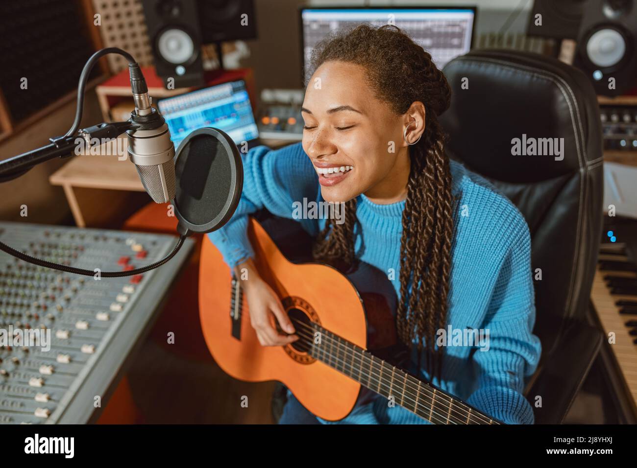 Enthusiastic multi-ethnic woman singer plays guitar and recordis song ...
