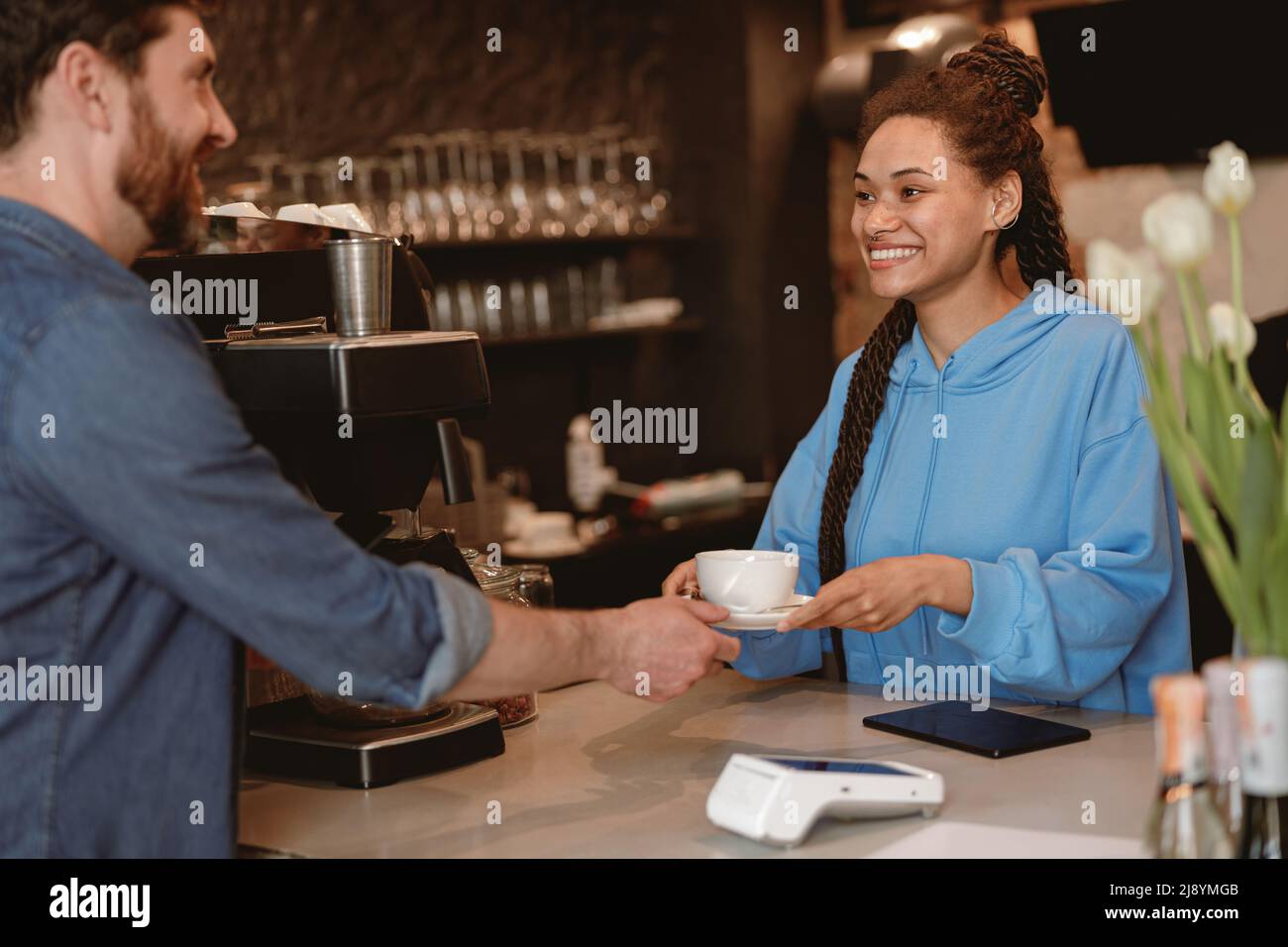 Cheerful young stylish waitress serving coffee to male client at bar ...