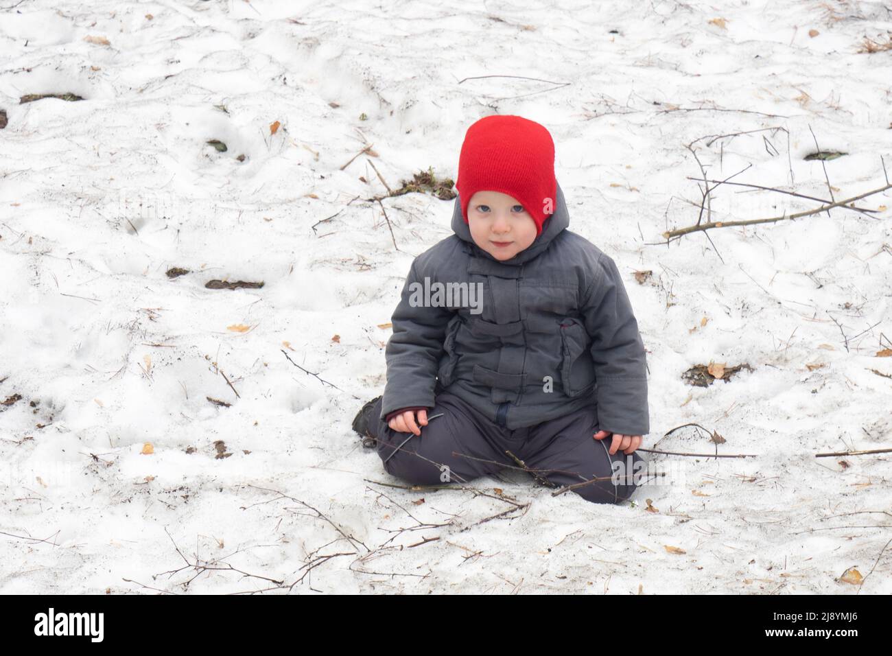 Small child in red cap and gray clothes sitting on knee in spring ...