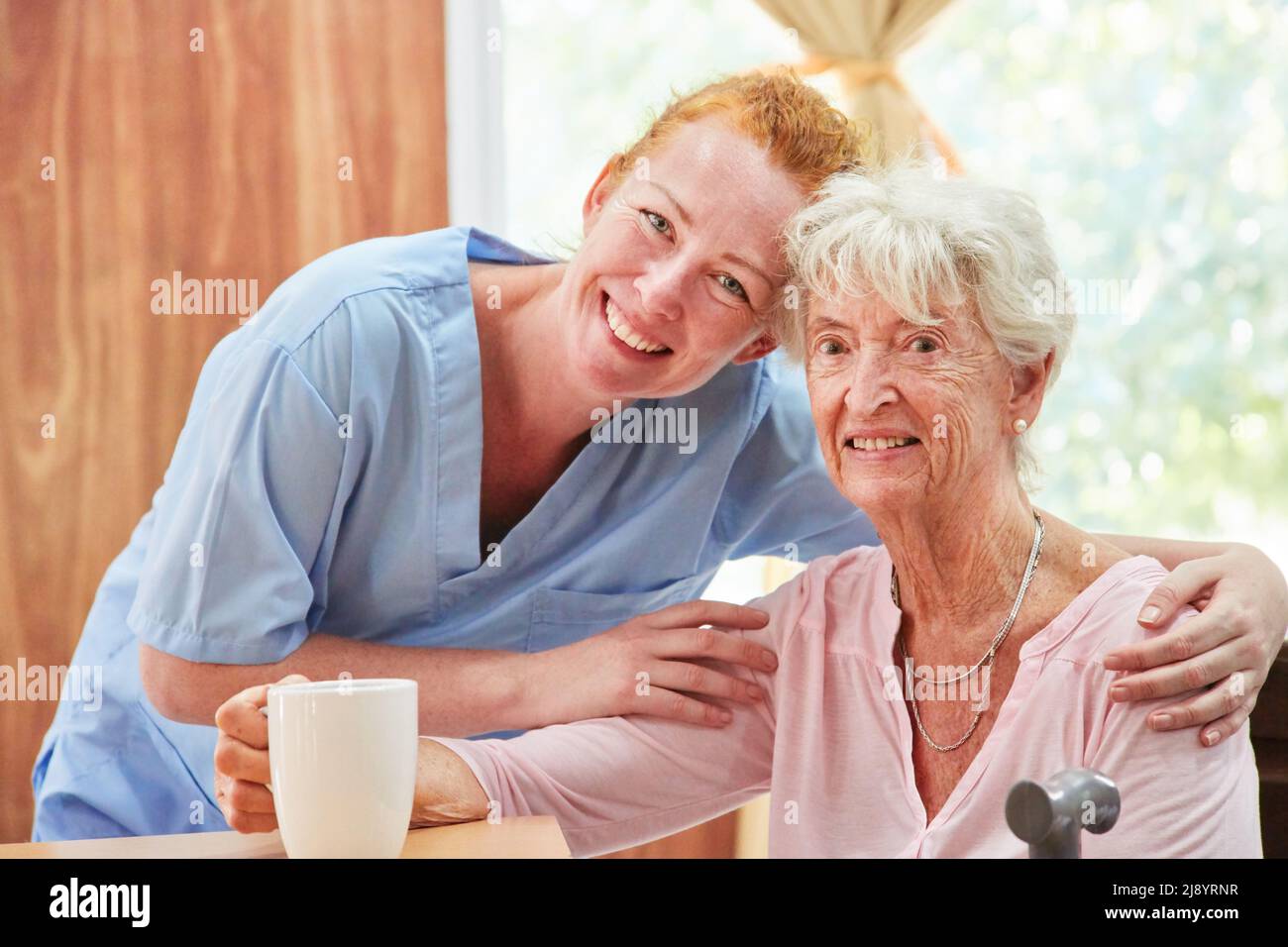 Smiling and caring caregiver and old woman together in nursing home or ...