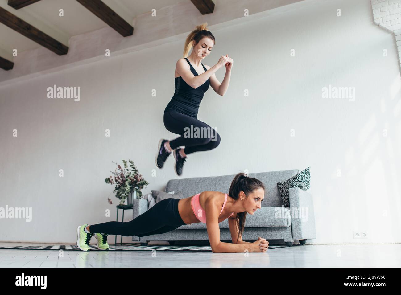 Fit women training home. Girl jumping over her friend while woman ...