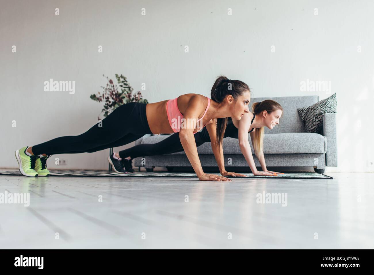 Two fitness women doing push-ups exercise working out at home. Side ...