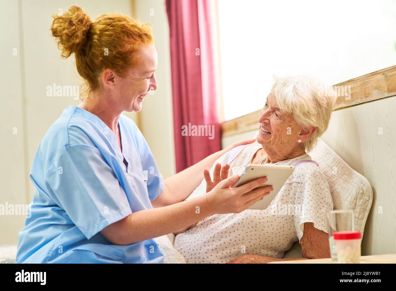 Elderly Nurse And Sick Senior Woman Look At Tablet Computer In Nursing
