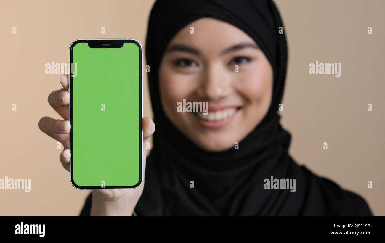 Portrait asian girl muslim islamic woman in black hijab smiling showing mobile phone with green ...