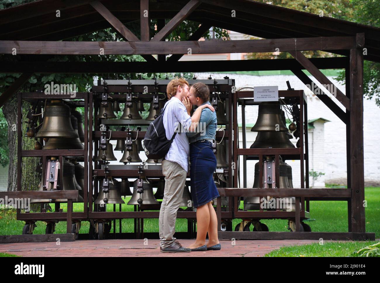 Young caucasian boy and girl kissing in a park, church bells set on a ...