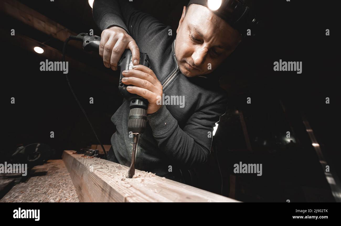 A man works with a drill in his workshop. Carpenter drills with a hand ...