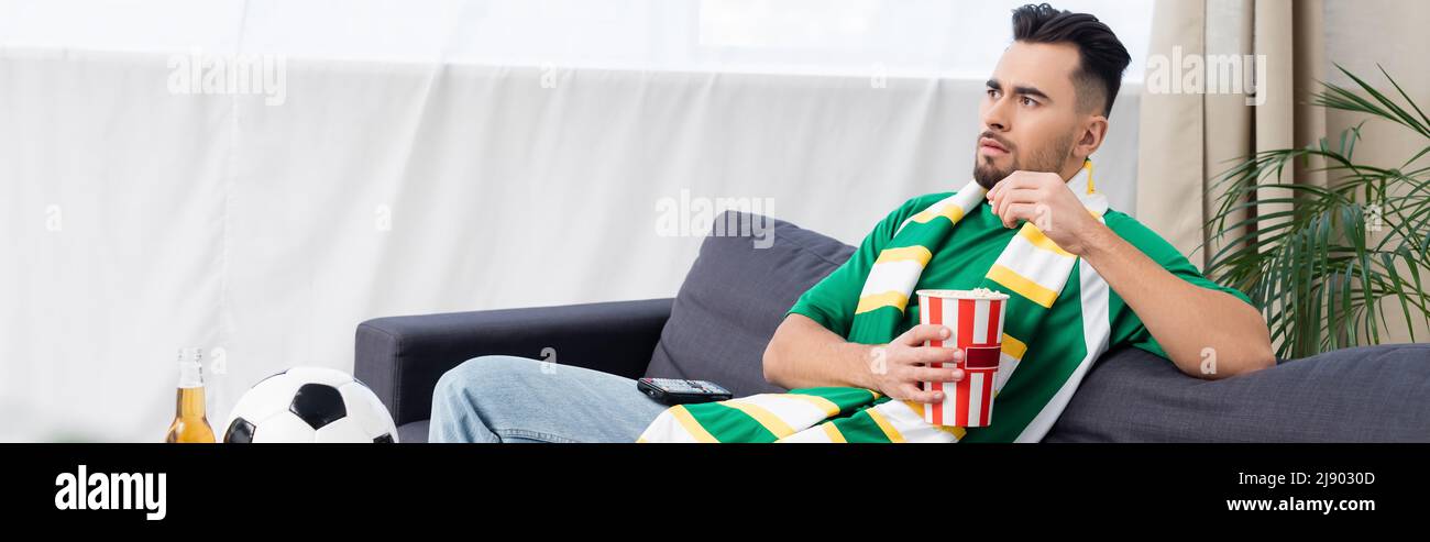 sports fan eating popcorn while watching game on tv near soccer ball ...