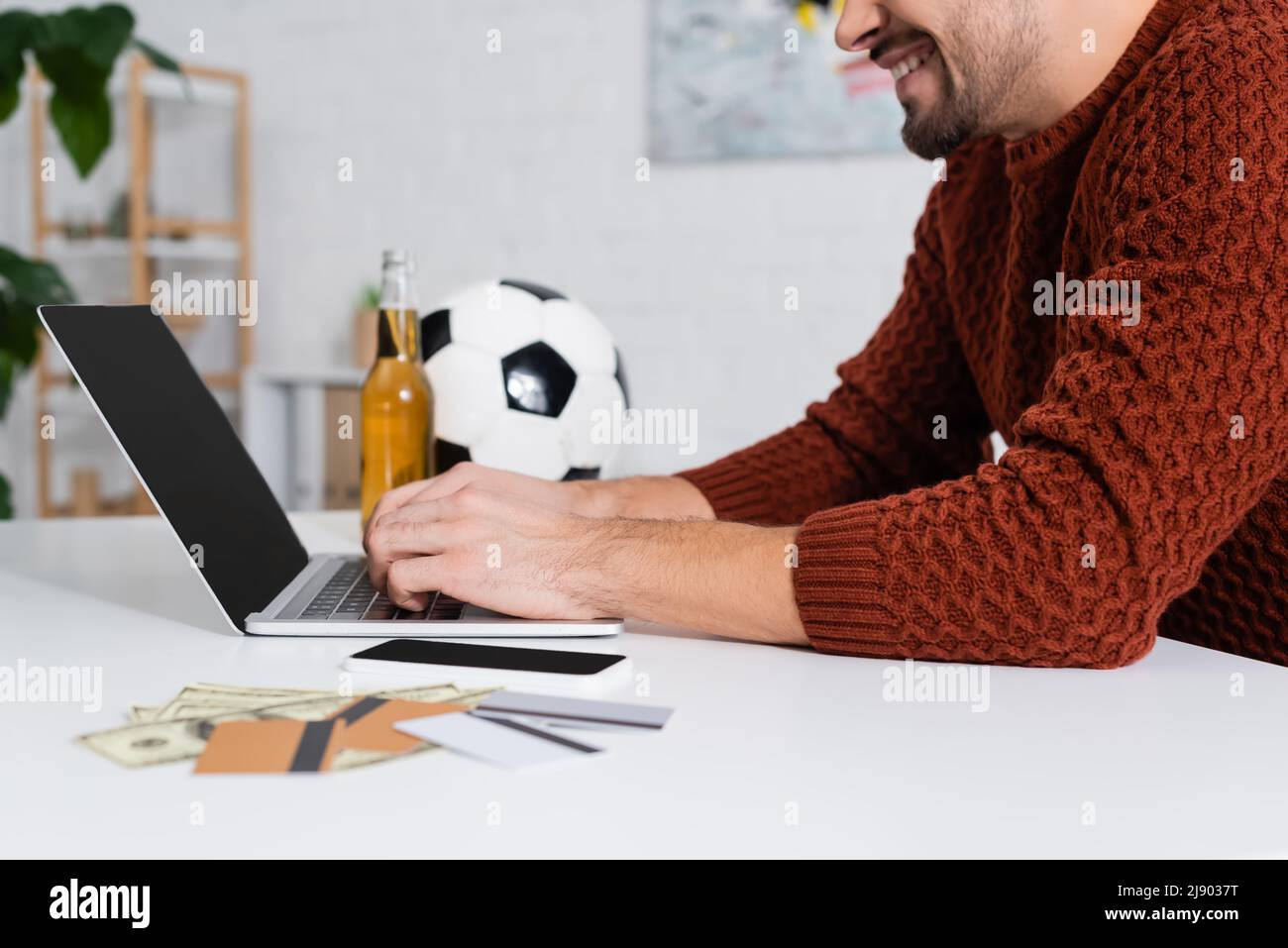 cropped view of smiling bookmaker typing on laptop near credit cards ...