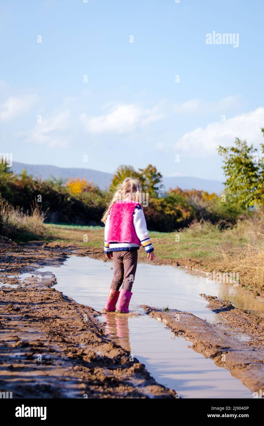 little lovely girl enjoying water puddle after rain in seasonal ...