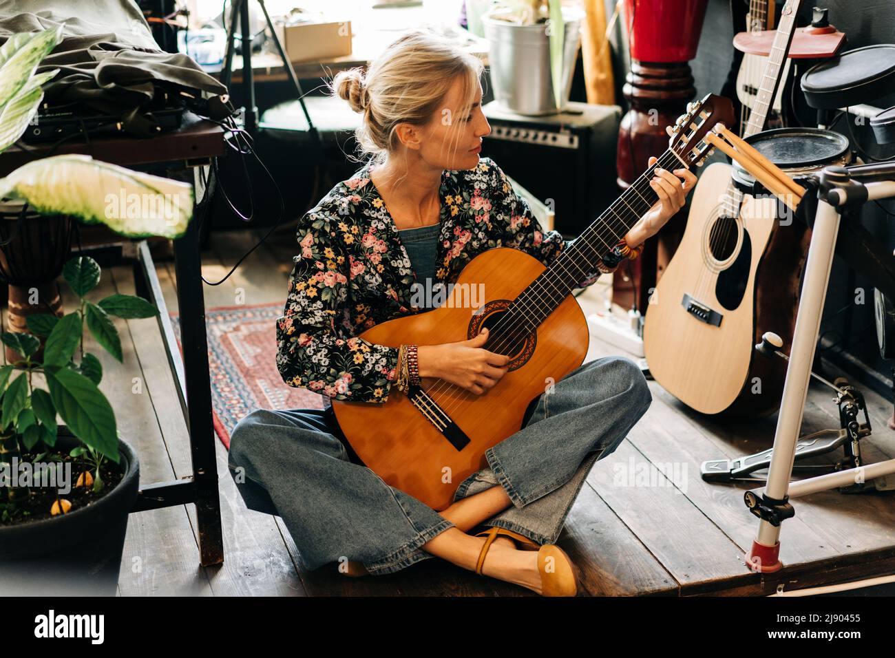 A woman plays an acoustic guitar while sitting on a stage among musical ...