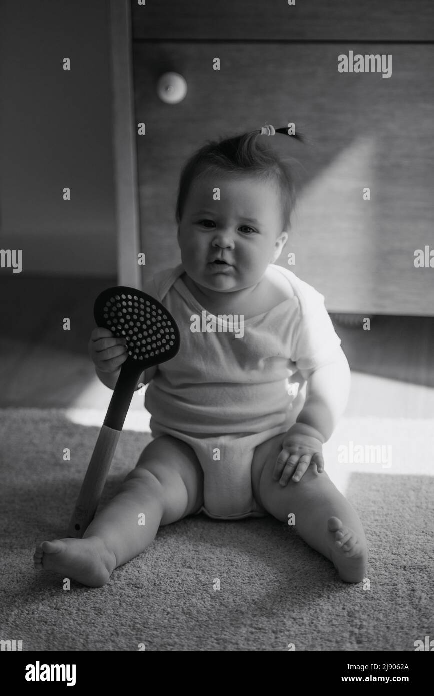 A black and white photo of a 7-month girl is sitting on the carpet ...