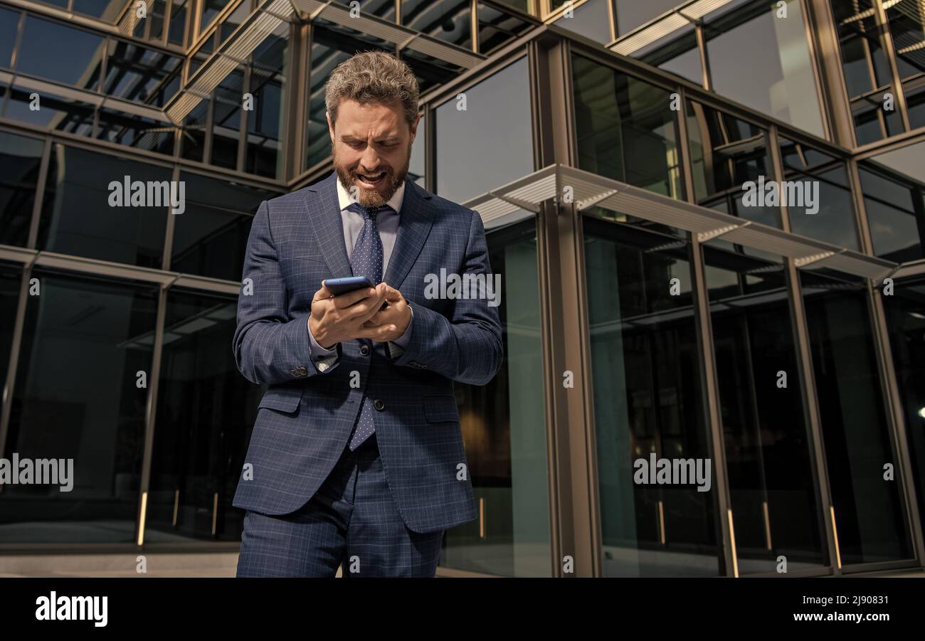 confused mature business man in formalwear holding phone outdoor, panic ...