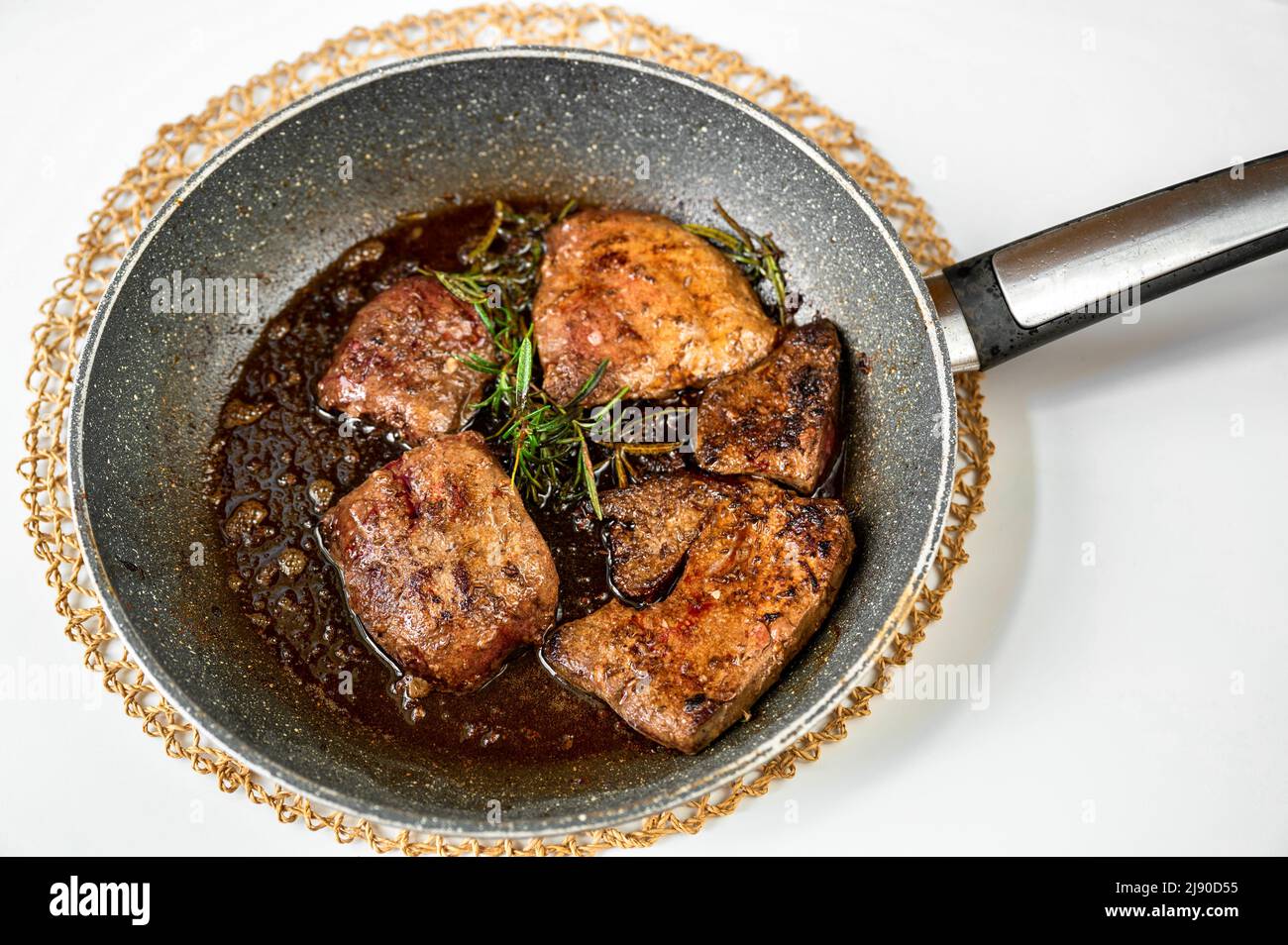 Fried sliced liver steak with rosemary herb in pan on white background ...