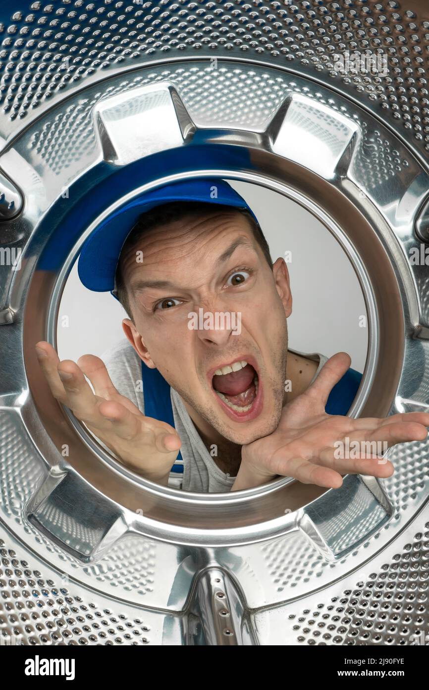 Angry screaming male repairman in uniform looks into the drum of the ...