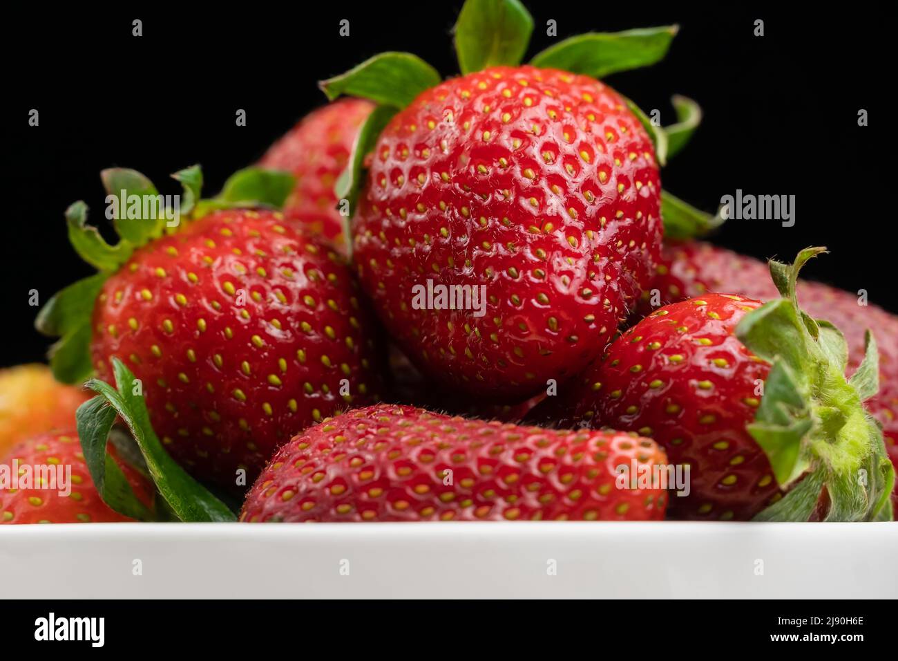 Close up ripe red strawberries with green tails in a white plate on a ...